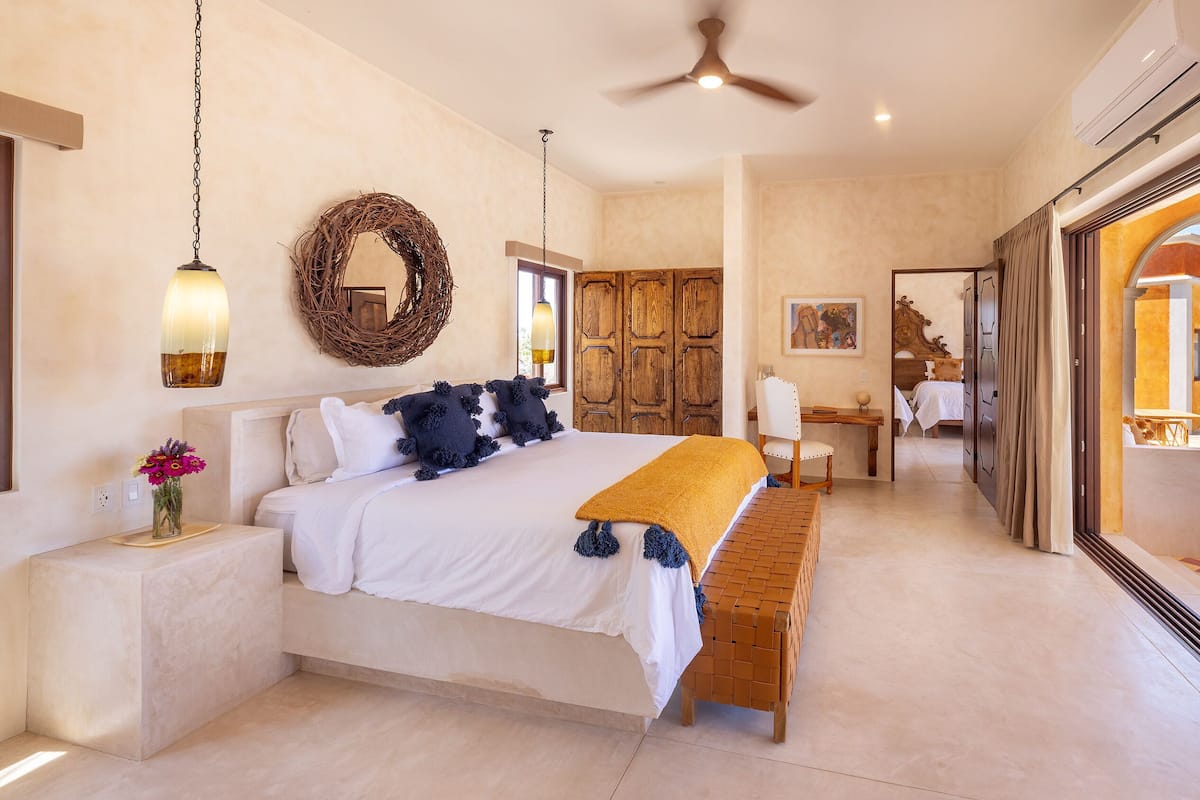 Um quarto espaçoso com uma cama grande, um banco de madeira, uma escrivaninha e vista para um pátio externo.