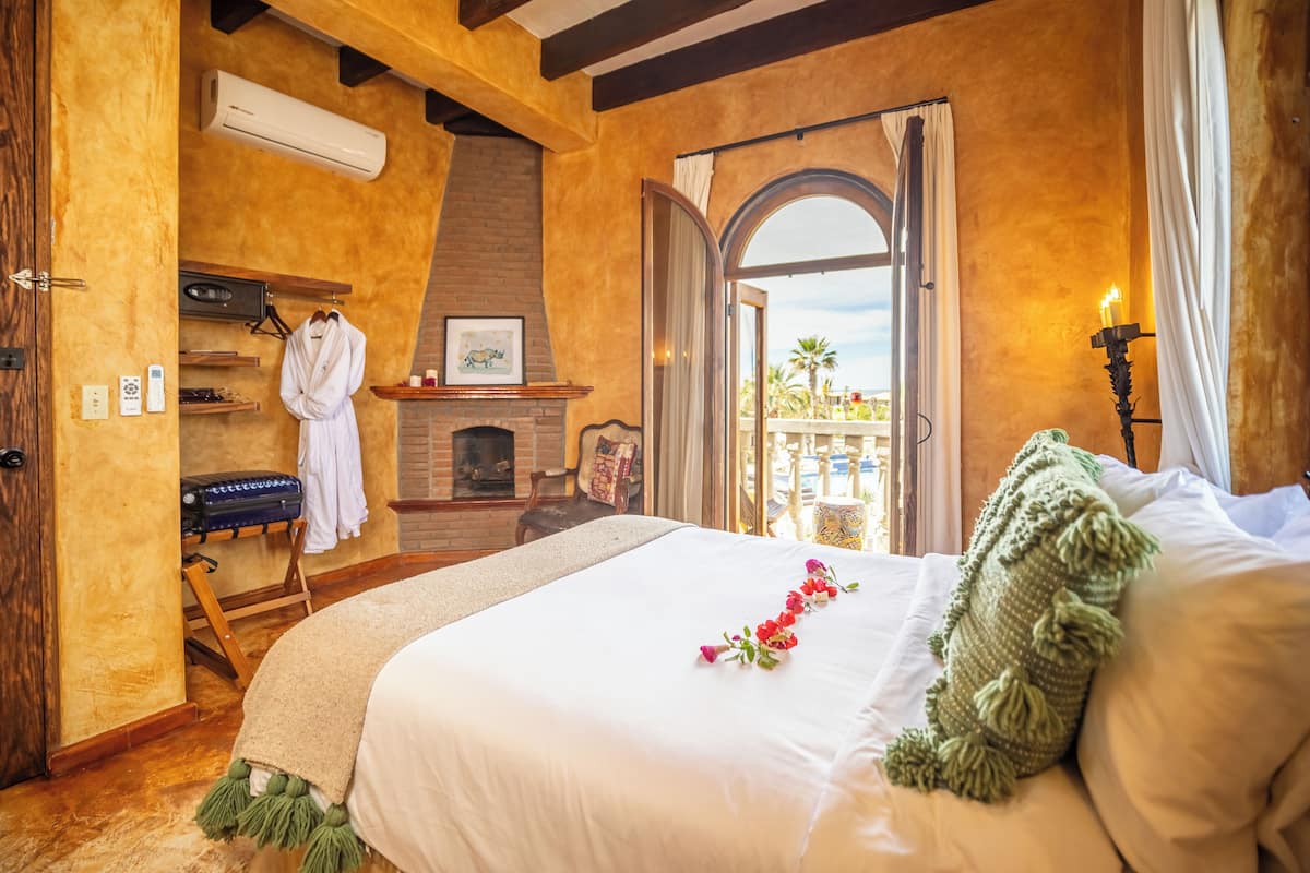 Quarto de hotel com cama, lareira, roupão e vista para o exterior.