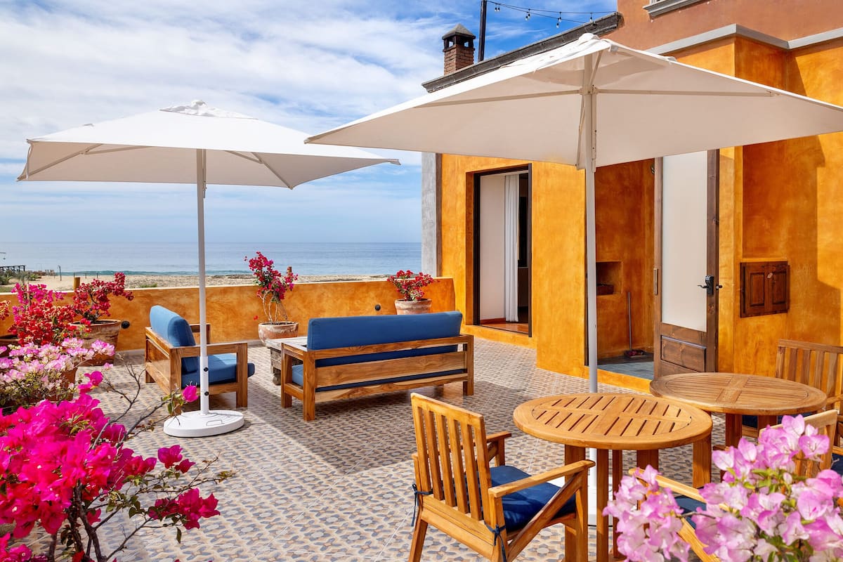 Um terraço com móveis de madeira, guarda-sóis brancos e plantas em vasos.