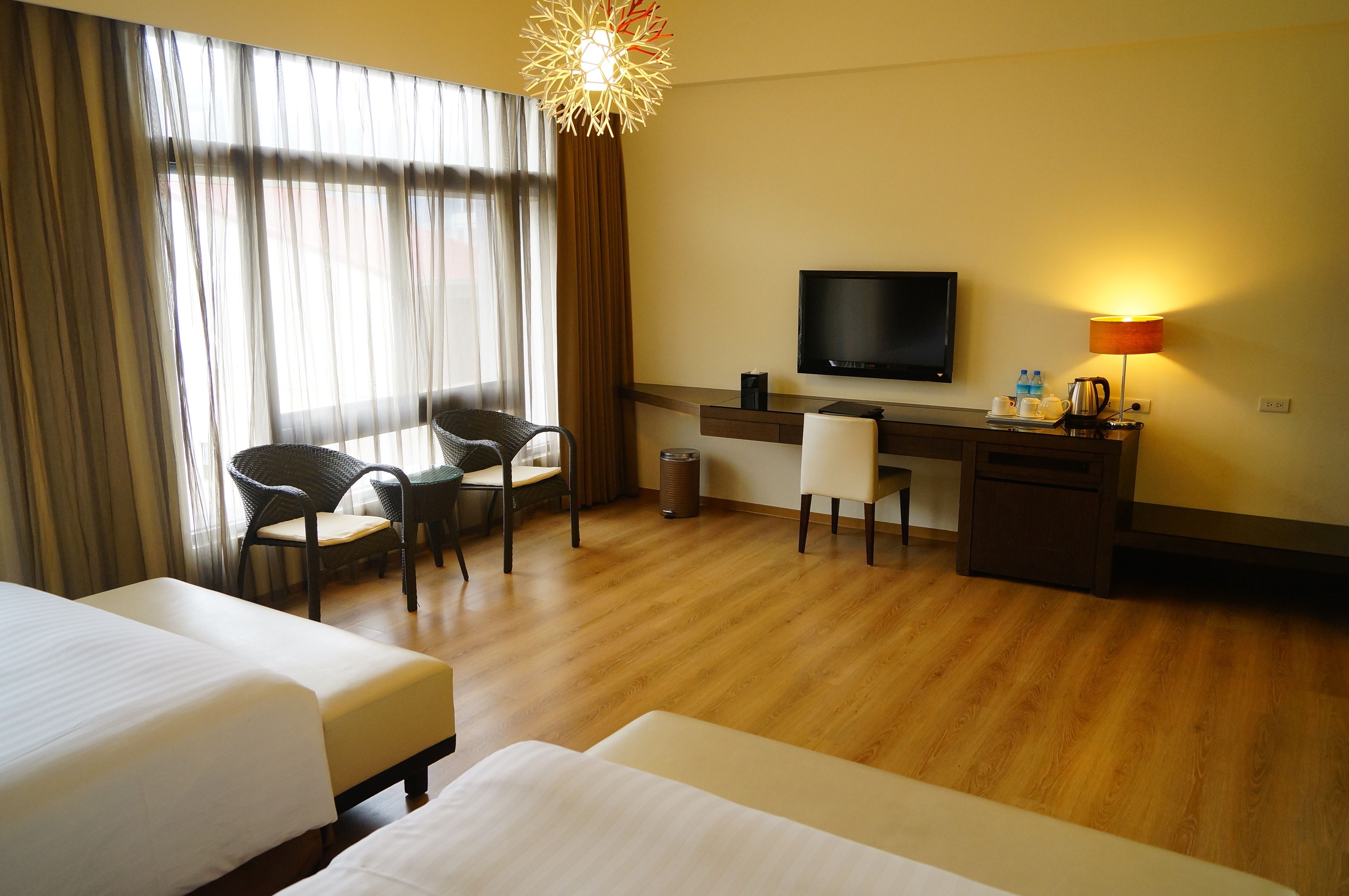 Quarto de hotel com duas camas, uma escrivaninha, uma cadeira, uma televisão e um abajur.