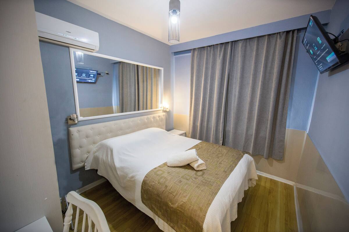 Quarto de hotel com cama, televisão fixada na parede e aparelho de ar condicionado.