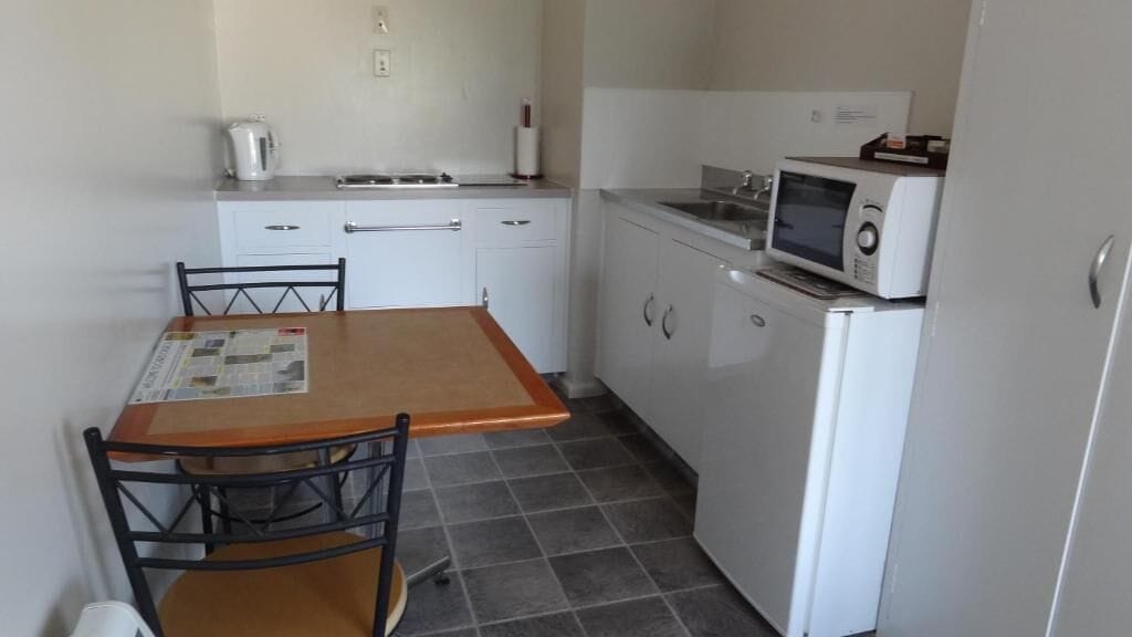 Uma cozinha compacta com mesa, cadeiras, micro-ondas e geladeira.
