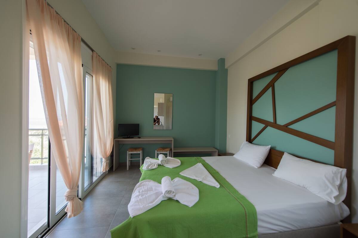 Quarto de hotel com cama, escrivaninha, cadeira e televisão.
