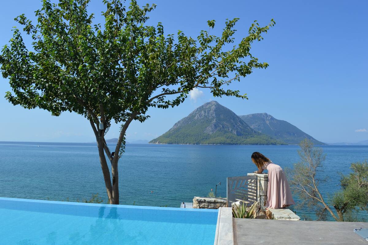 Área da piscina com vista para o mar e uma montanha ao fundo.