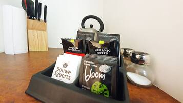 Uma bandeja com café, saquinhos de chá, chaleira e um pote de creme.