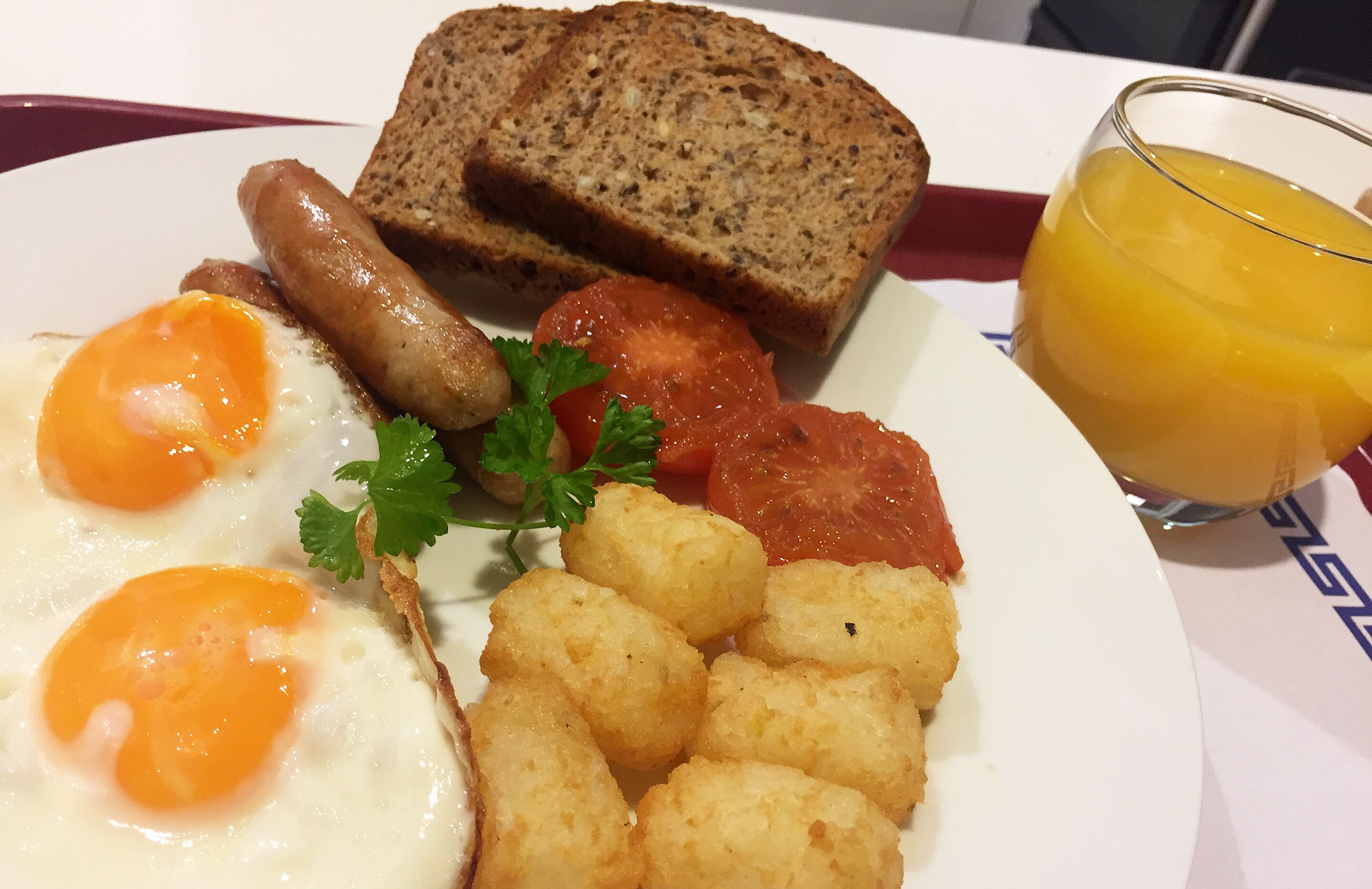 Um prato com ovos, salsichas, torradas, tomates e mini-batatas.