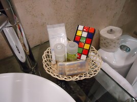 Uma bancada de banheiro com produtos de higiene pessoal, incluindo escova de dentes, creme dental, dosador de sabonete e um pequeno frasco de loção.