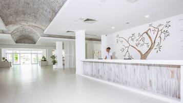 Um hall amplo com balcão de recepção, um mural com tema de árvore e teto alto com design texturizado.