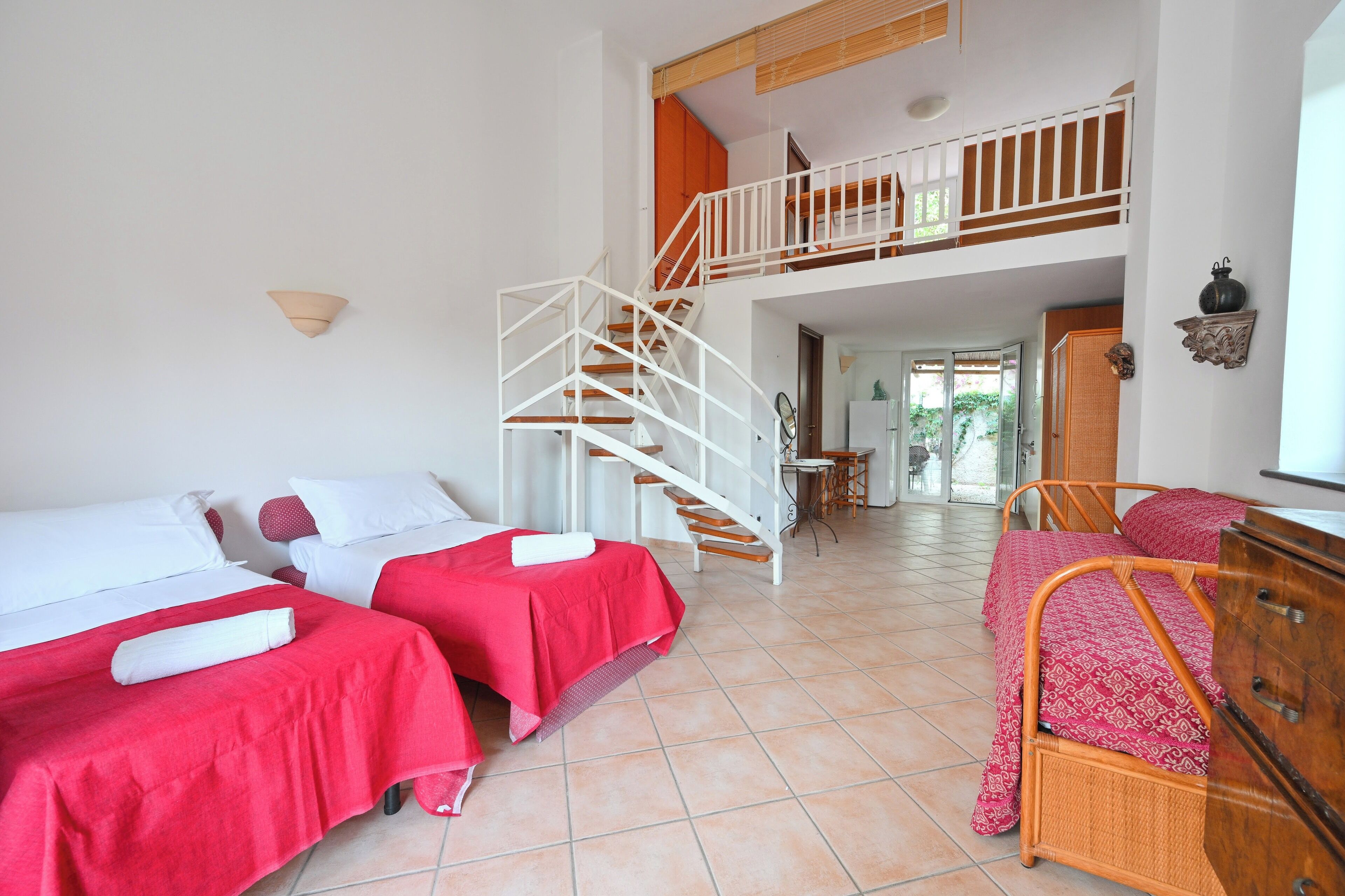 Quarto de hotel com duas camas, penteadeira de madeira, escada e vista para o exterior.