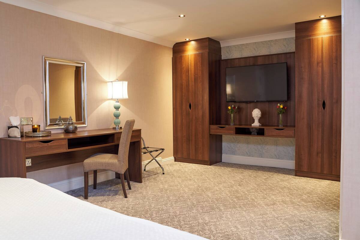 Quarto de hotel com cama, escrivaninha e cadeira, espelho grande, televisão de tela plana e armários de madeira.