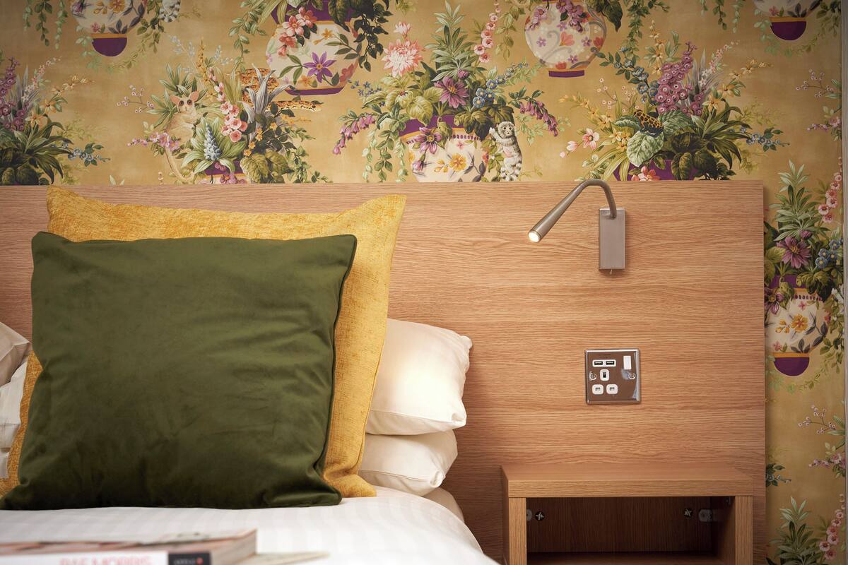 Cama bem arrumada com travesseiro verde e amarelo, um travesseiro branco e um livro intitulado "Rae Morris" na lateral.