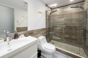 Casa de banho moderna com cabine de chuveiro em vidro, lavatório branco e sanita.