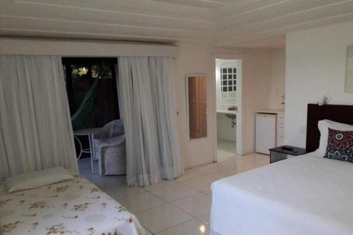 Quarto de hotel com duas camas, uma pequena escrivaninha, uma cadeira e vista para o exterior.
