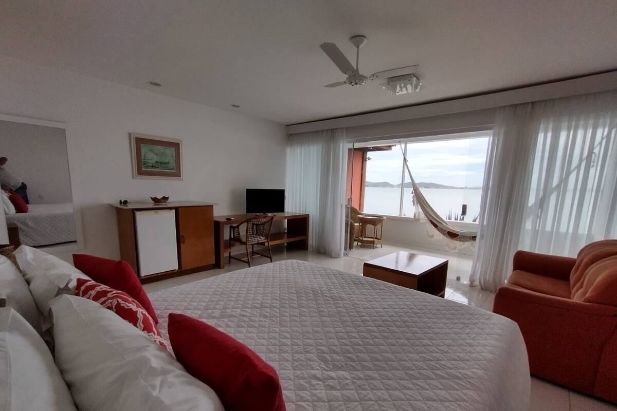 Quarto de hotel com cama, escrivaninha, cadeira, TV e vista para o mar.