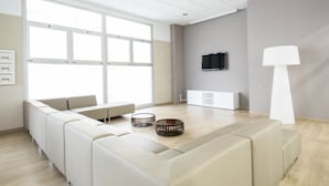 Uma sala de estar moderna com sofá seccional, duas mesas de centro, televisão de tela plana na parede e um abajur.