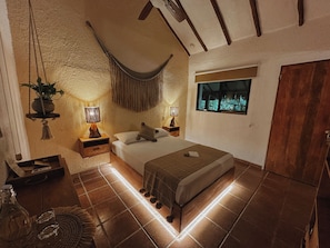 Quarto com cama, mesas de cabeceira, luminárias, planta pendente e janela com vista.