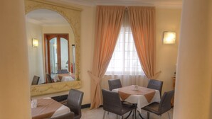 Uma sala de jantar de hotel com uma mesa posta para quatro pessoas, rodeada por cadeiras, e um espelho grande refletindo o espaço.