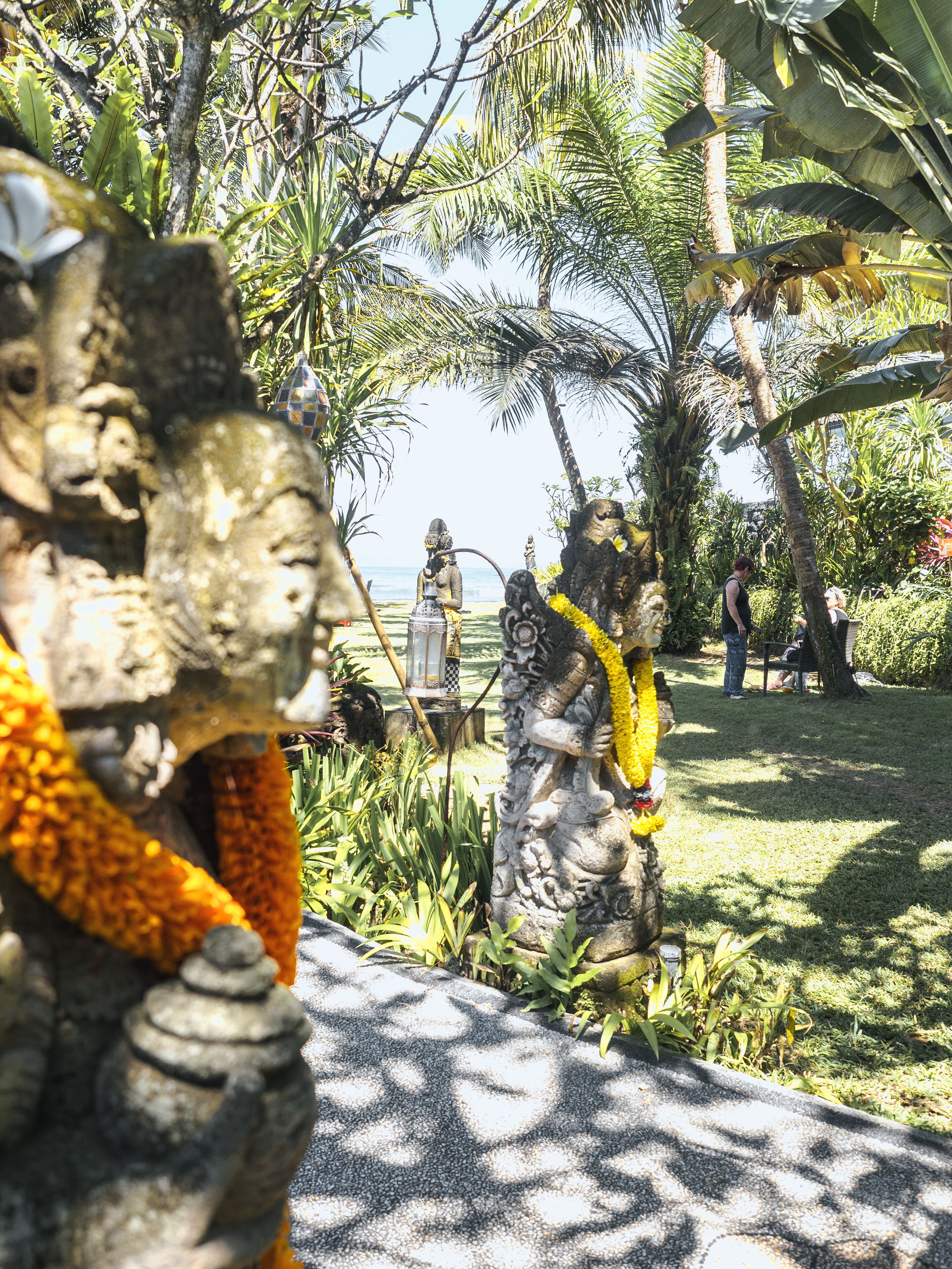 Um jardim com estátuas, incluindo um elefante grande e uma estátua de mulher segurando uma flor amarela.