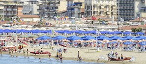 Uma praia com vários guarda-sóis e espreguiçadeiras, um barco e pessoas a desfrutar da costa.