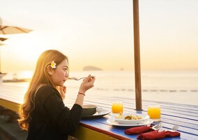 Alguém jantando à mesa com vista para o mar e um pôr do sol.