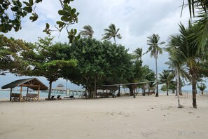 Uma praia com palmeiras, um quiosque de madeira e uma rede de voleibol.