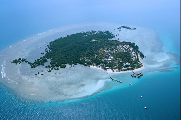 Vista aérea de uma ilha tropical com águas turquesa cristalinas, uma praia arenosa e vegetação exuberante.