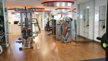 Uma academia com diversos equipamentos de exercício, piso de madeira e um espelho grande na parede.