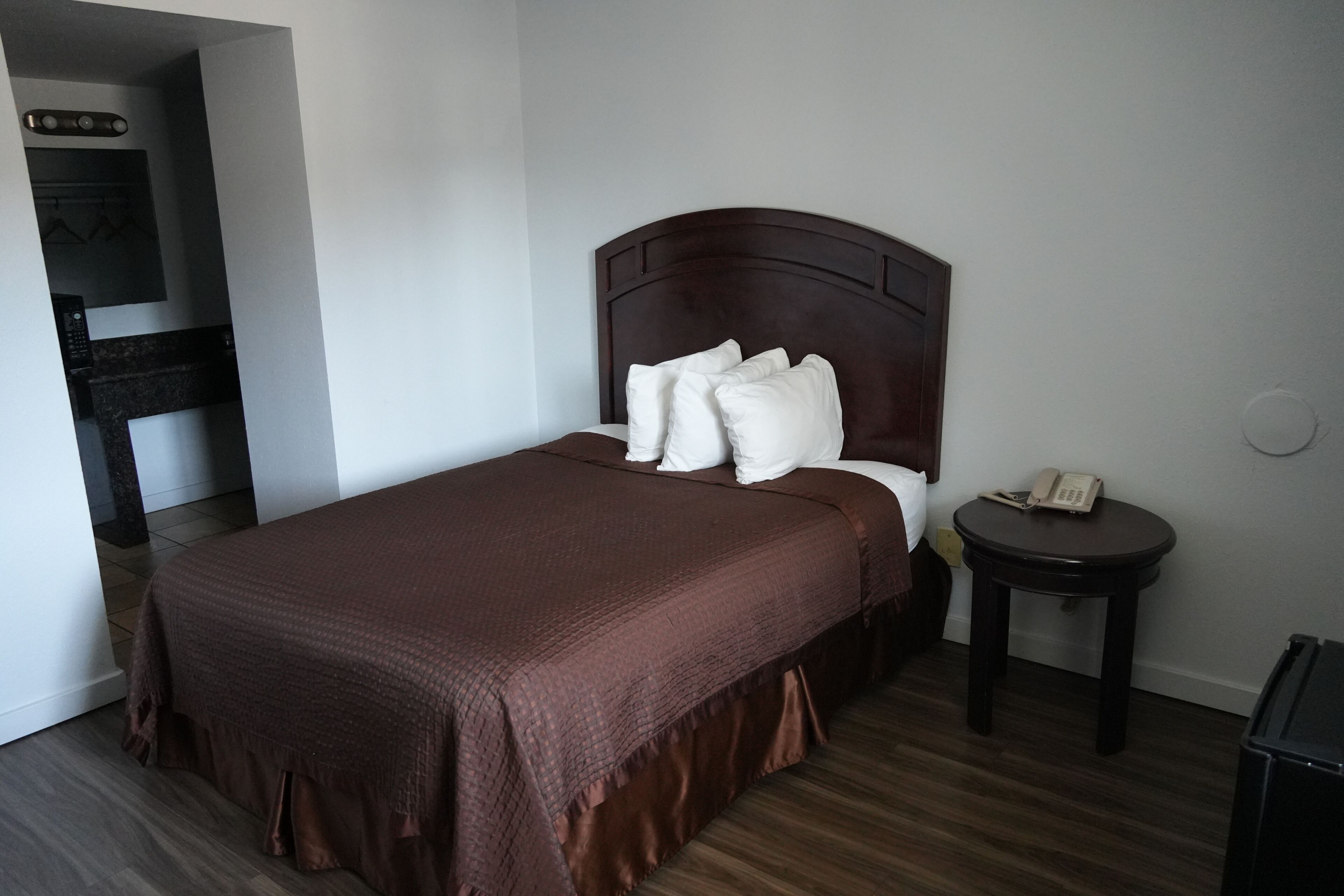 Quarto de hotel com cama, mesa de cabeceira com telefone e pequena mesa com abajur.