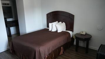 Quarto de hotel com cama, mesa de cabeceira com telefone e pequena mesa com abajur.