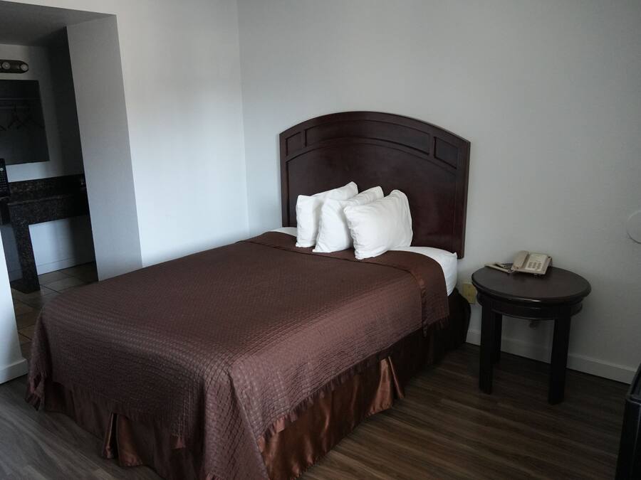 Quarto de hotel com cama, mesa de cabeceira com telefone e pequena mesa com abajur.