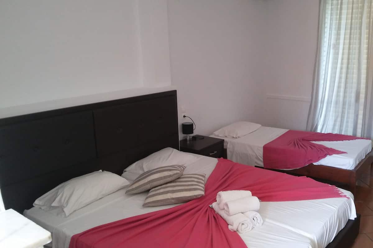 Quarto de hotel com duas camas, cada uma com roupa de cama branca e detalhes vermelhos. Há uma mesa de cabeceira com abajur entre as camas.