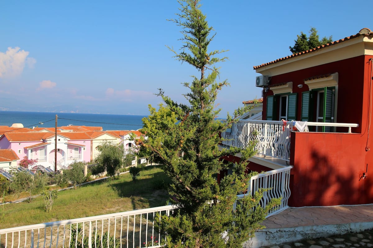 Uma área residencial costeira com casas, uma árvore de pinheiro imponente e uma vista clara do mar.