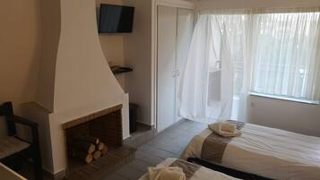 Quarto com duas camas, lareira, TV fixada na parede e janela com cortinas leves.