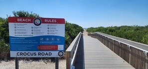Placa de regras da praia numa passarela de madeira que leva à praia.