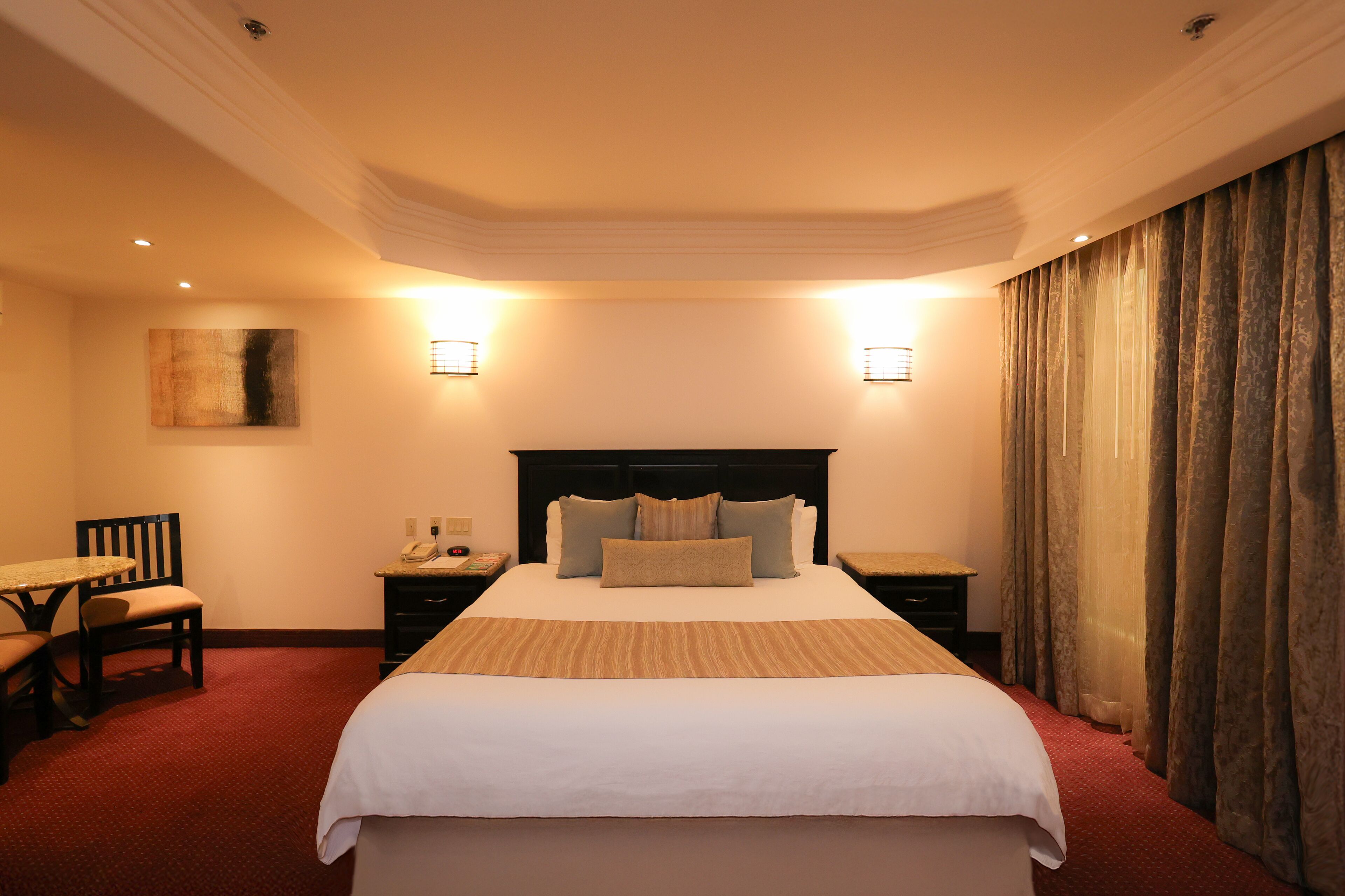 Quarto de hotel com uma cama grande, uma escrivaninha, uma cadeira e uma mesa de cabeceira com abajur.