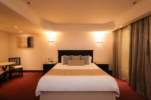 Quarto de hotel com uma cama grande, uma escrivaninha, uma cadeira e uma mesa de cabeceira com abajur.