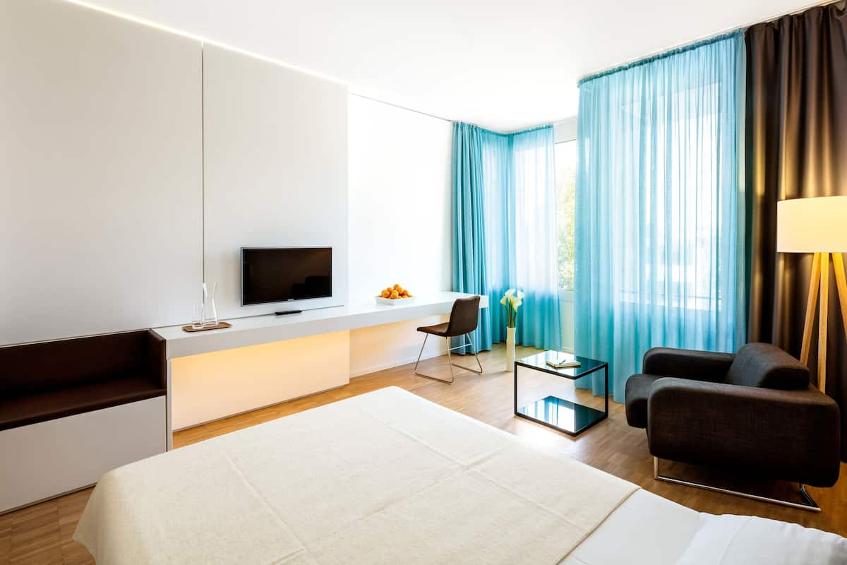 Quarto de hotel moderno com cama, televisão, escrivaninha e área de estar.