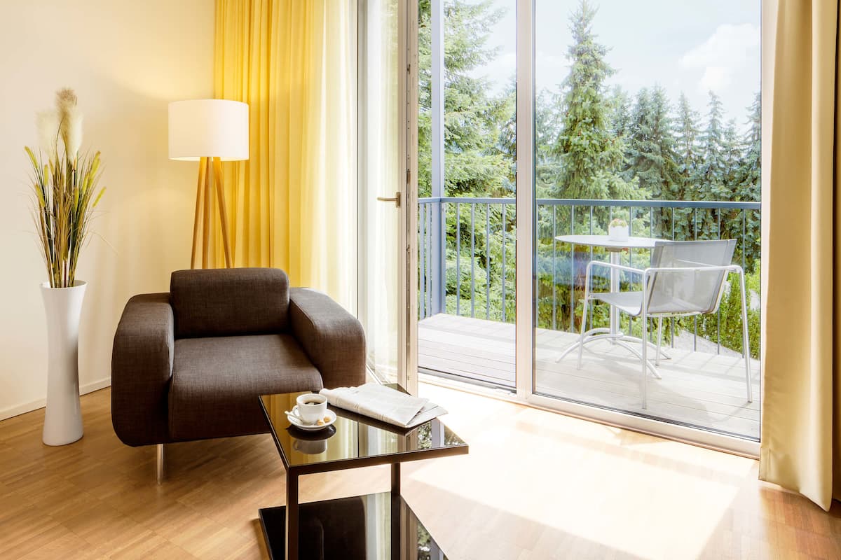 Uma sala de estar moderna com um sofá, uma mesa de centro de vidro e vista para uma varanda com mobiliário exterior.