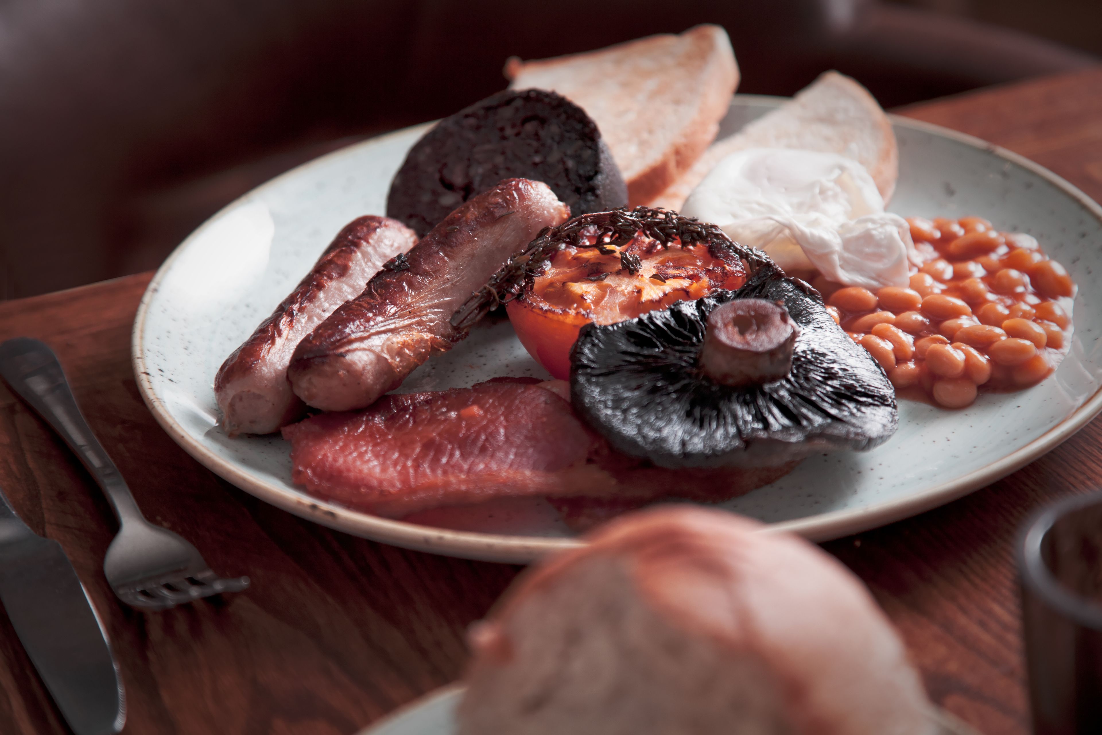 Um prato com linguiça, uma fatia de pão e feijão cozido.
