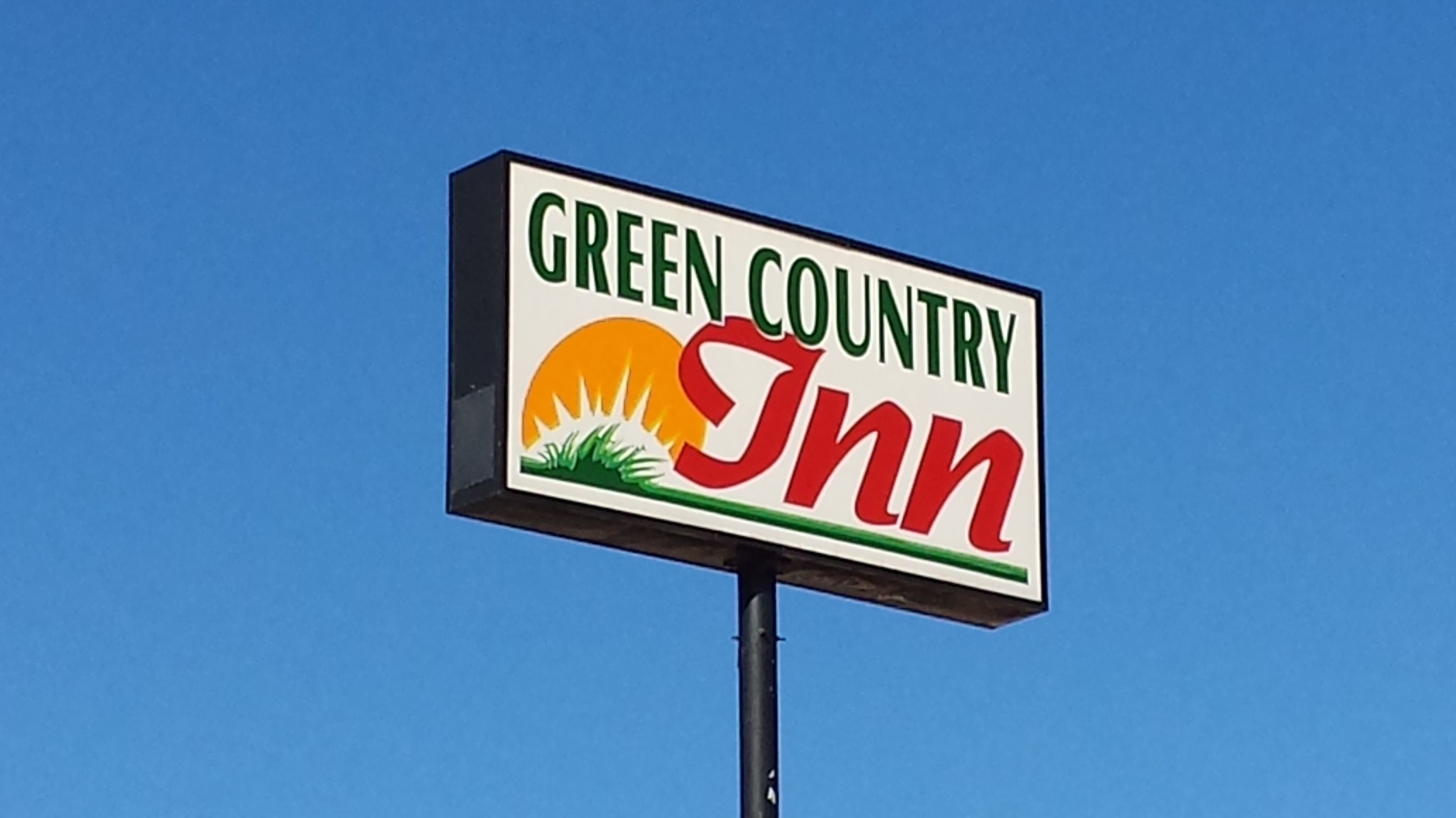 Placa do Green Country Inn com um céu claro ao fundo.