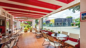 Restaurante com mesas ao ar livre, decoração em vermelho e branco e vista para a rua.