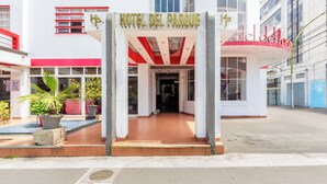 A entrada do Hotel Del Parque, com fachada em vermelho e branco, acesso coberto e vasos com plantas em primeiro plano.