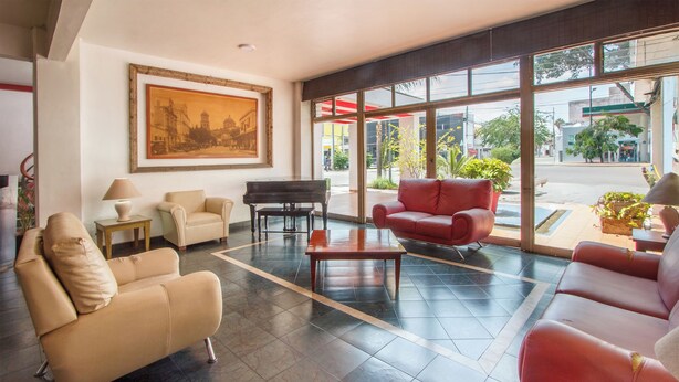 Um hall amplo com um piano, sofás de couro, uma mesa de centro e uma janela grande com vista para a rua.