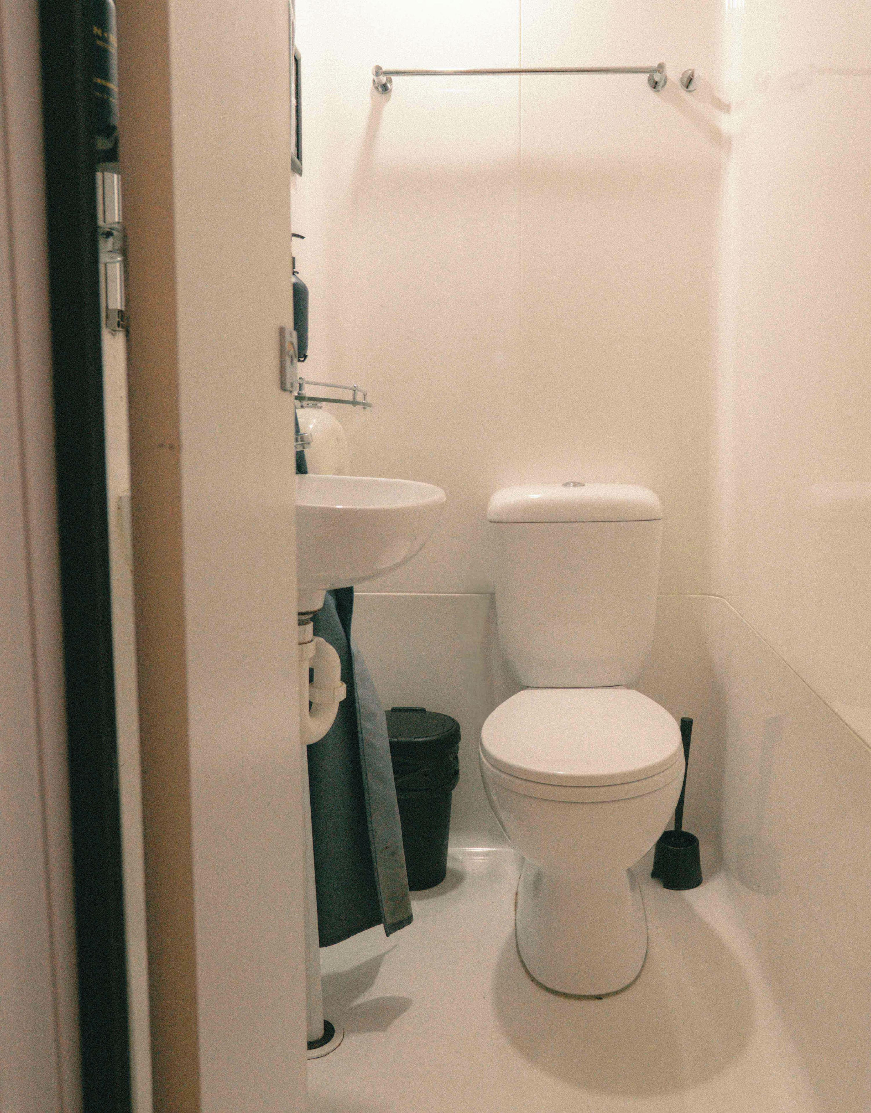Casa de banho pequena e compacta, com sanita, lavatório e um contentor de lixo.