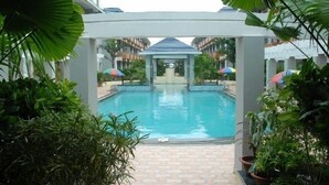 Piscina com um coreto no centro, rodeada por plantas em vasos e guarda-sóis.