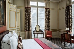 Quarto de hotel com cama, escrivaninha, cadeira e janela com cortinas.