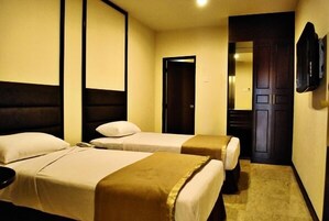 Quarto de hotel com duas camas, uma cabeceira de madeira escura, uma televisão de tela plana fixada na parede e piso coberto de carpete.