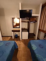 Um quarto pequeno com beliches, uma televisão, uma escrivaninha com espelho e um pequeno frigorífico.