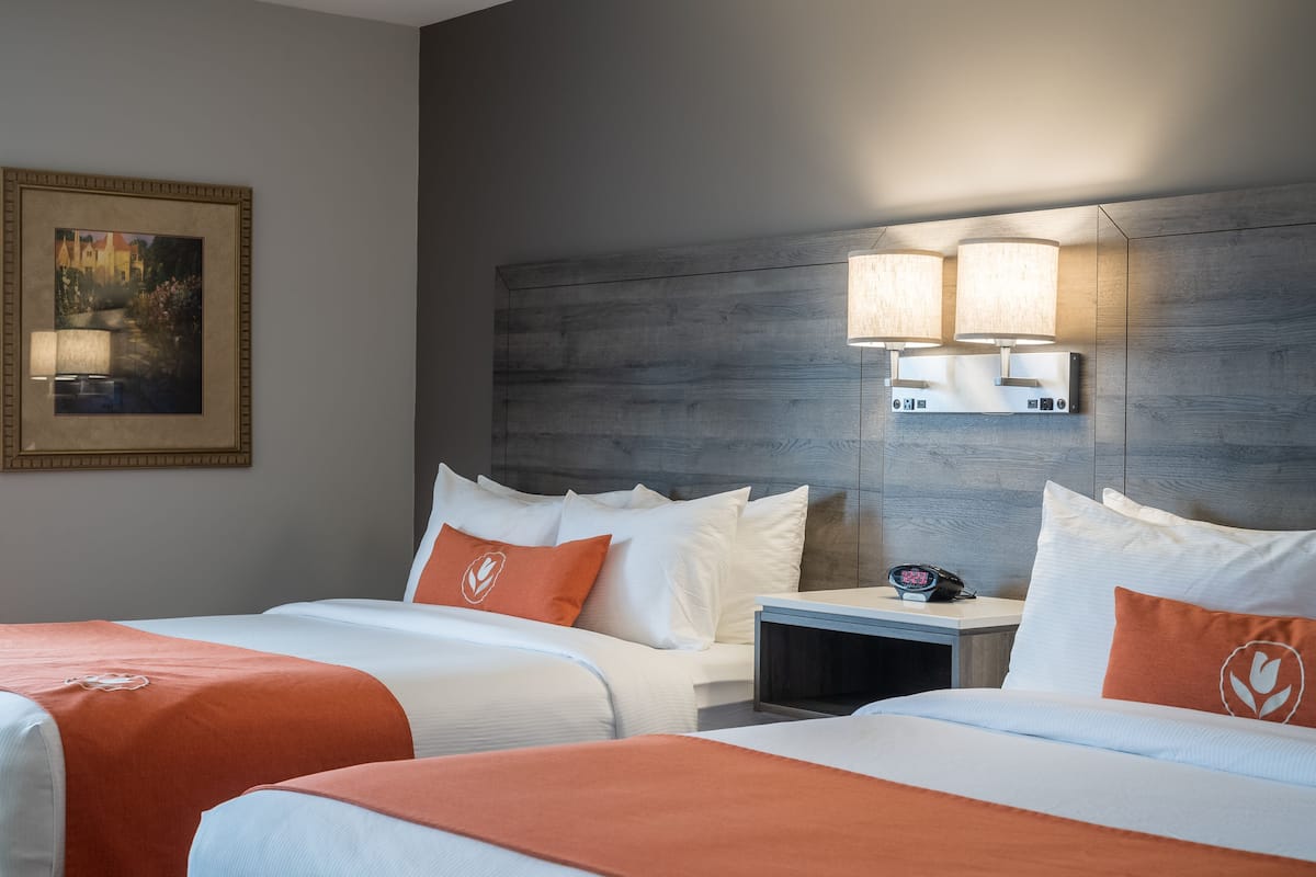 Quarto de hotel com duas camas, mesa de cabeceira, abajur e um quadro pendurado na parede.