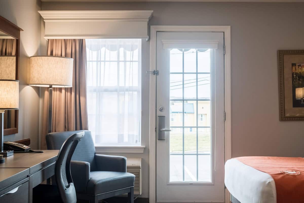 Quarto de hotel com escrivaninha, cadeira, cama e janela com cortinas.